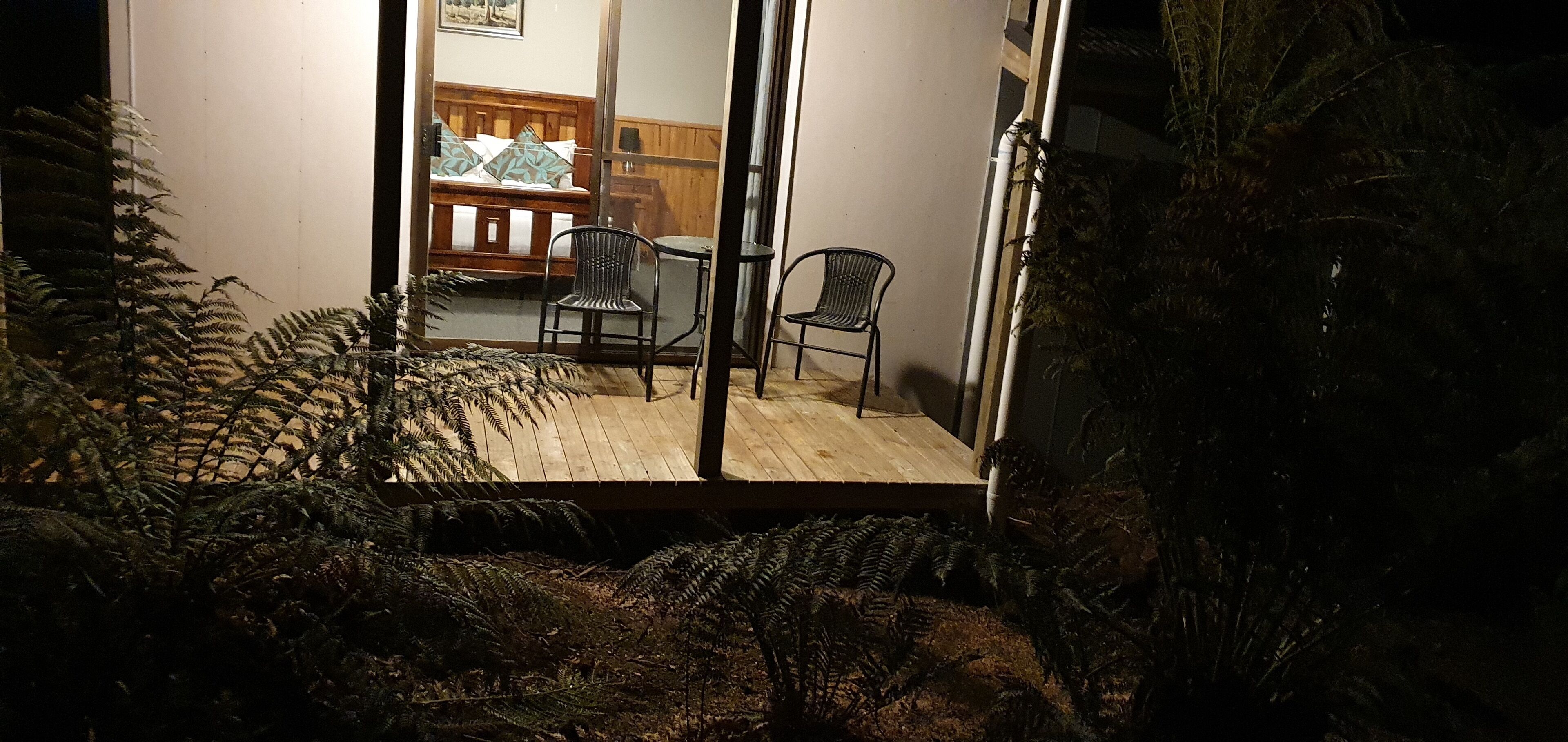 Quarto com deck de madeira, duas cadeiras e cama com almofadas estampadas.