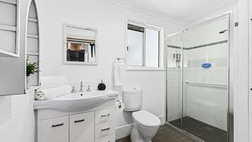Casa de banho moderna com lavatório, sanita e chuveiro, tudo em branco.