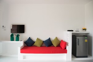 Uma sala de estar moderna com um sofá vermelho, almofadas coloridas, uma TV de tela plana e uma geladeira.