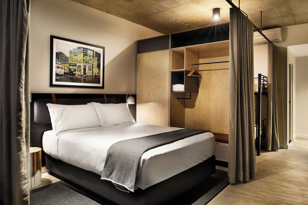 Quarto de hotel moderno com uma cama grande, um guarda-roupa, um quadro emoldurado na parede e um cabideiro.