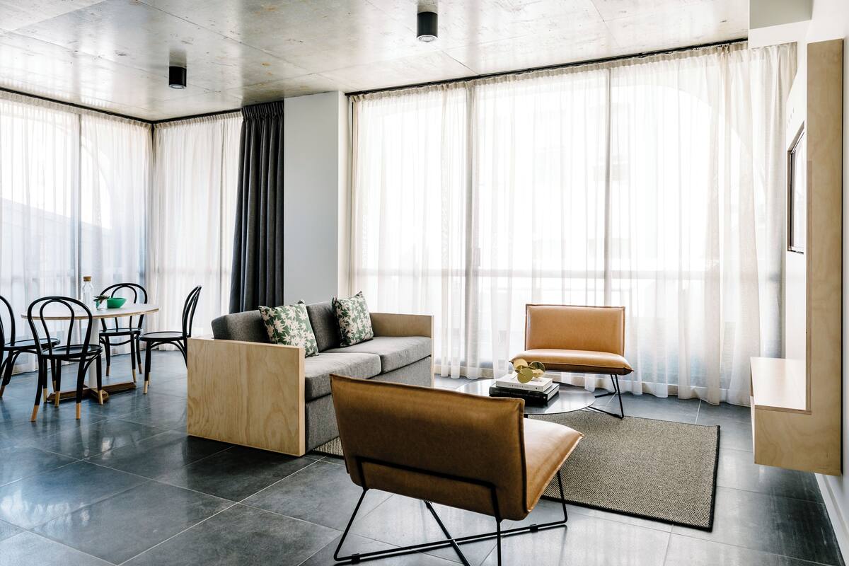 Uma sala de estar moderna com sofá, poltronas e um espaço de jantar com cadeiras e mesa.