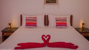Uma cama bem arrumada com lençóis brancos e duas almofadas, uma listrada e outra lisa, em um quarto com cabeceira e mesas de cabeceira de madeira simples.