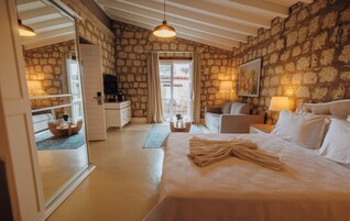 Um quarto aconchegante com parede de pedra, uma cama com toalhas bem dobradas, uma mesinha de madeira e uma cadeira.