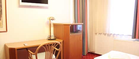 Quarto de hotel com cama, escrivaninha, cadeira, televisão e janela com cortinas.