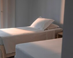 Uma cama de solteiro com colchão e travesseiro brancos em um quarto com parede lisa e janela com cortinas.