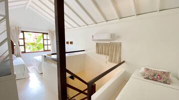 Um quarto espaçoso com teto alto, uma cama com travesseiro floral, uma janela com cortinas e um ar condicionado branco.