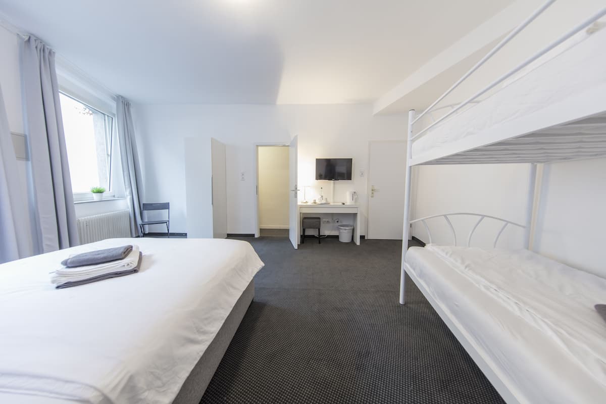 Quarto de hotel com cama, escrivaninha, cadeira, televisão e janela com cortinas.