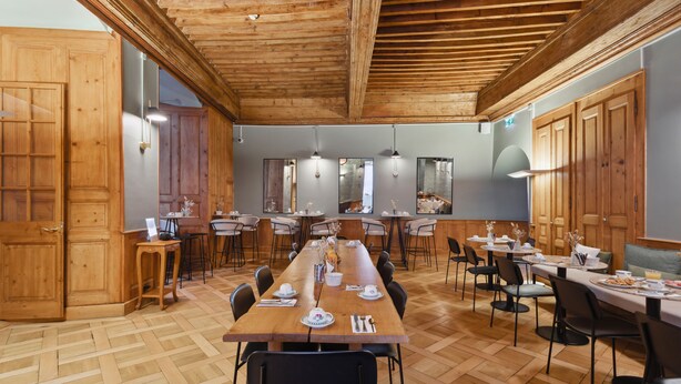 Uma ampla sala de jantar com mesas e cadeiras de madeira, um balcão comprido e armários de madeira.