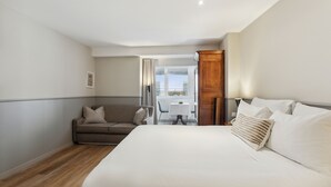 Quarto de hotel com uma cama grande, um sofá, um guarda-roupa de madeira e vista para a varanda.