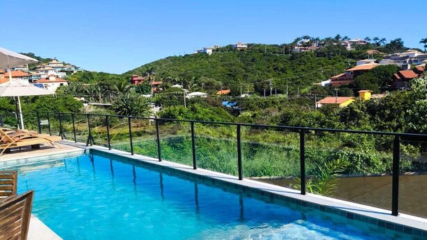Piscina com água azul cristalina, rodeada por um deck ladrilhado e guarda-corpo preto.