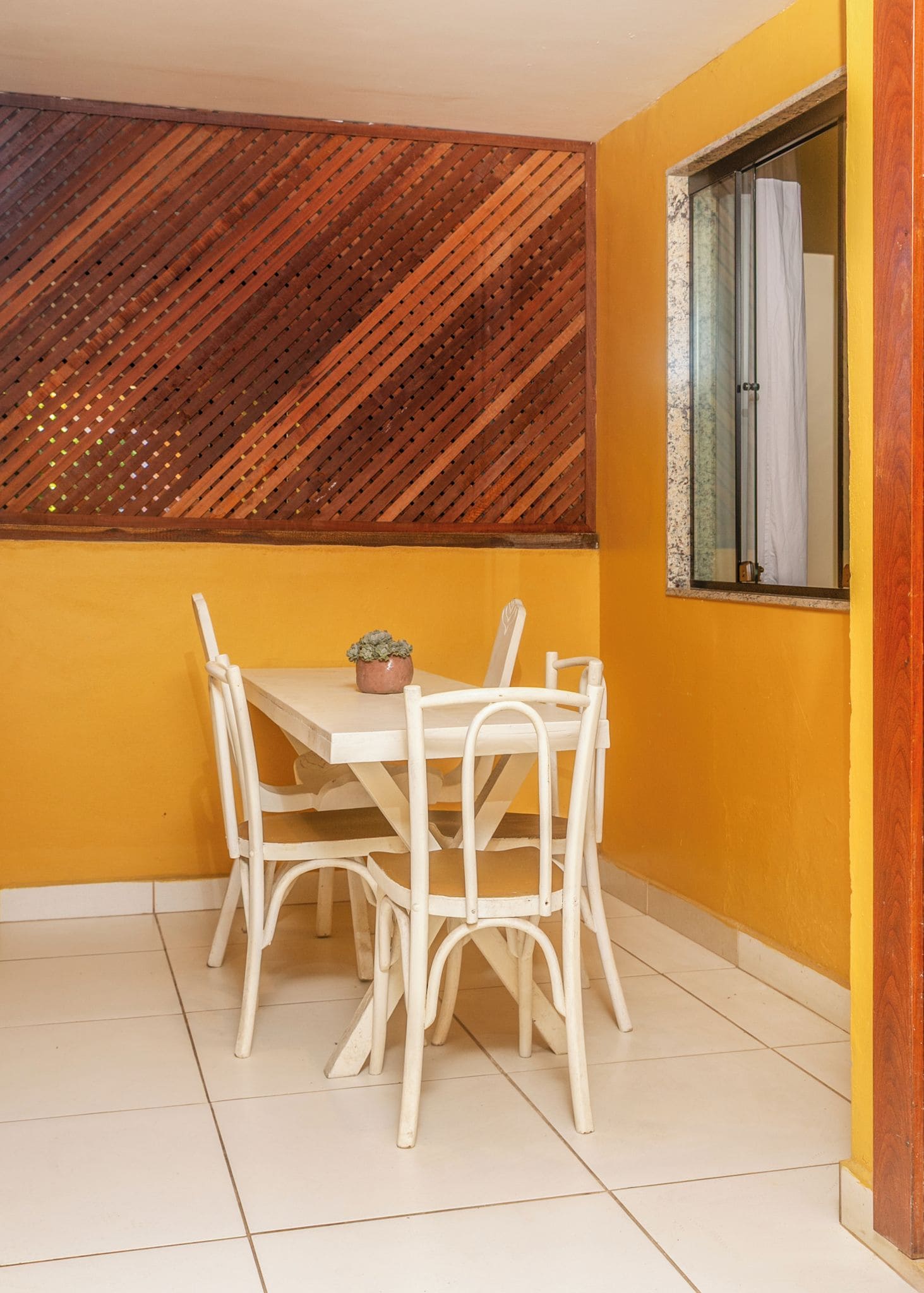 Uma área de refeições com mesa, cadeiras, planta em vaso e janela com cortinas.