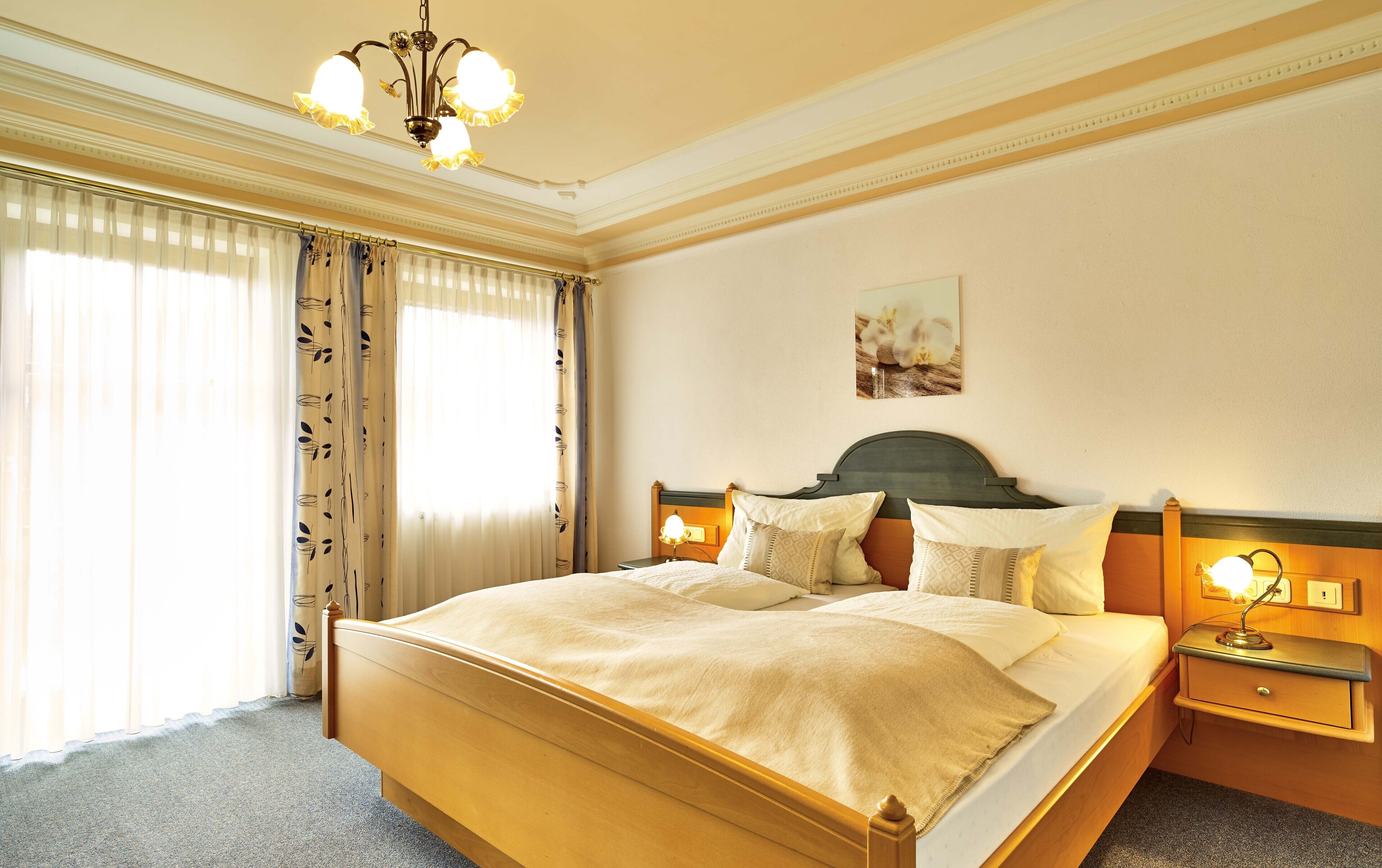 Quarto de hotel com uma cama grande, um candelabro, uma mesa de cabeceira com abajur e um quadro na parede.