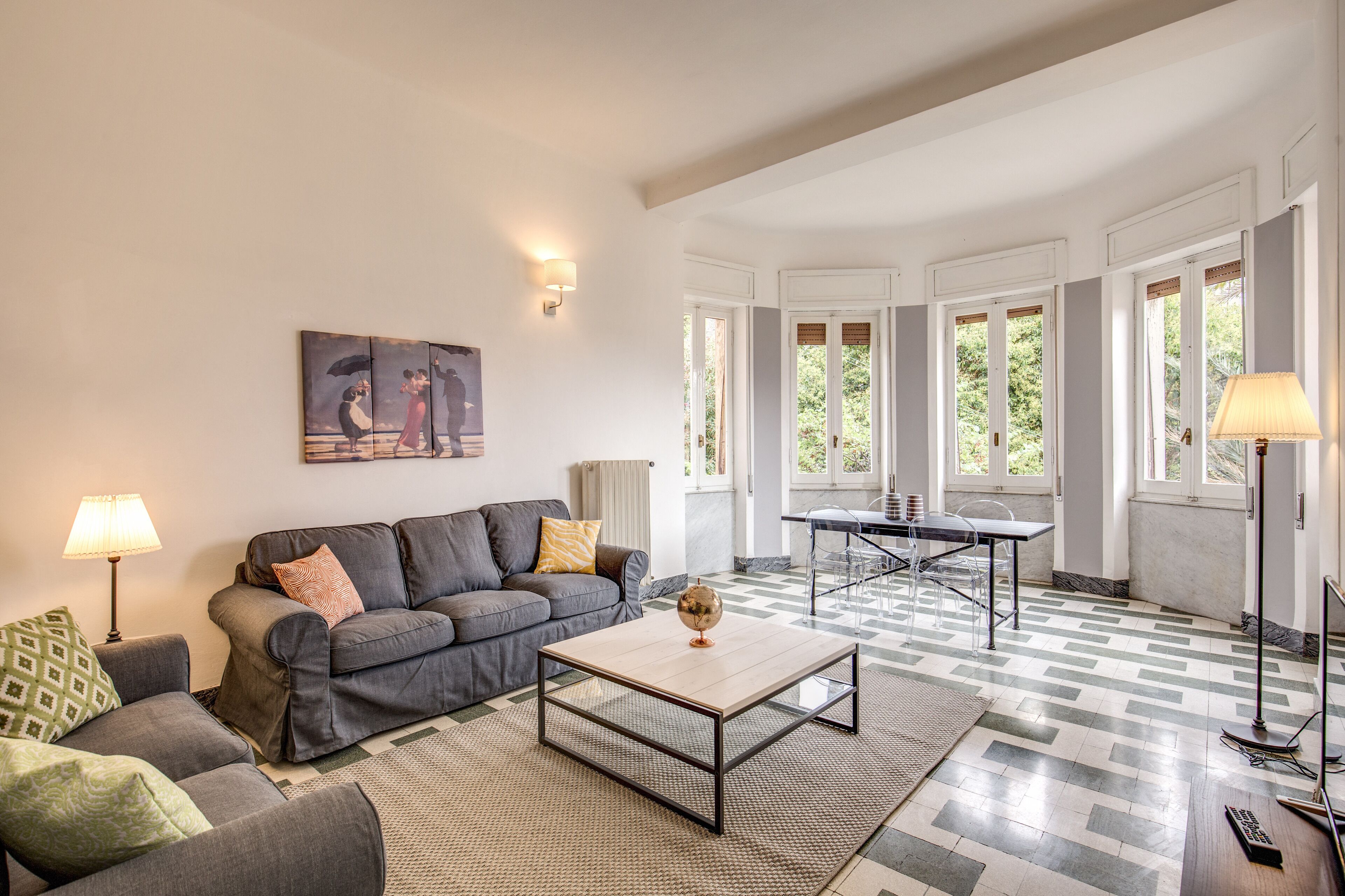 Uma sala de estar com um sofá cinzento, uma mesa de centro e um quadro na parede.