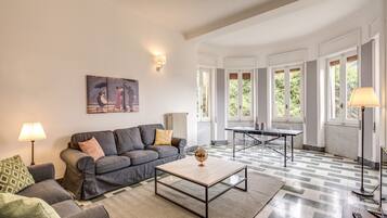 Uma sala de estar com um sofá cinzento, uma mesa de centro e um quadro na parede.