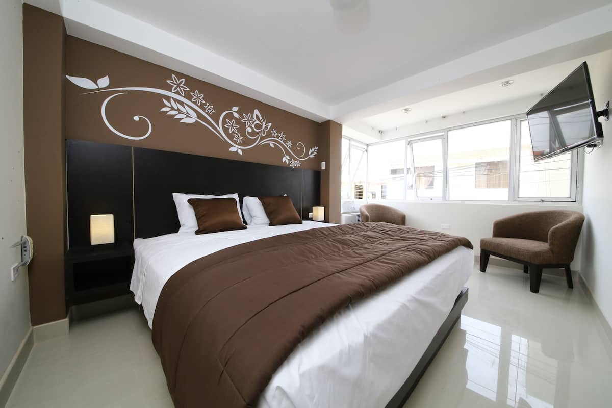 Quarto de hotel moderno com uma cama grande, televisão de tela plana na parede e uma janela com vista para o exterior.