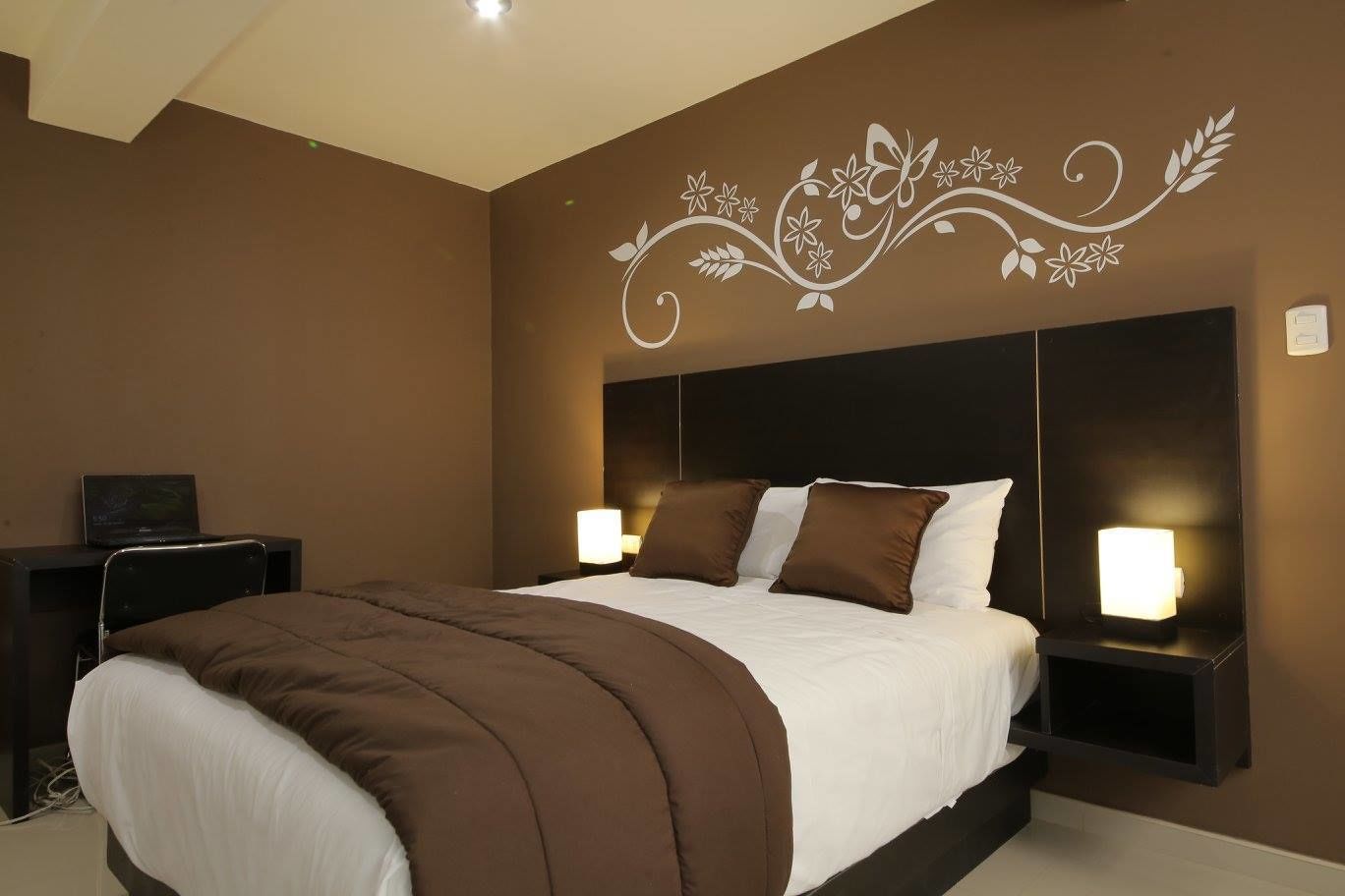 Quarto com cama grande, duas mesas de cabeceira, um laptop em uma escrivaninha e arte decorativa na parede.