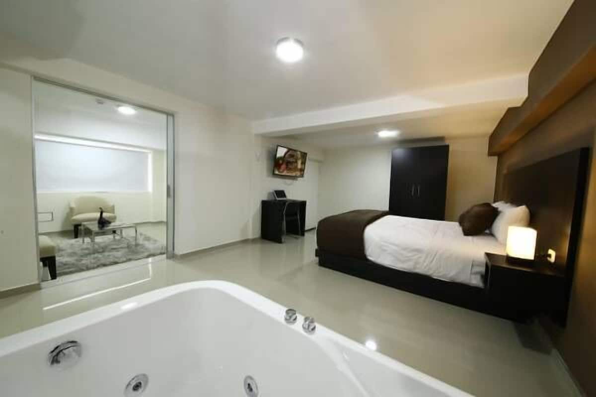 Quarto moderno com uma cama grande, mesa de cabeceira com abajur, televisão e uma banheira espaçosa.