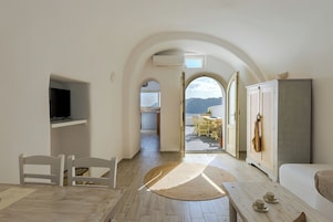 Quarto com televisão, área de refeições com cadeiras e mesa, guarda-roupa e vista para o mar.