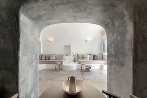 Um interior moderno com um arco de pedra, uma área de estar central com sofás e uma mesa de centro, e um vaso sobre uma mesa.