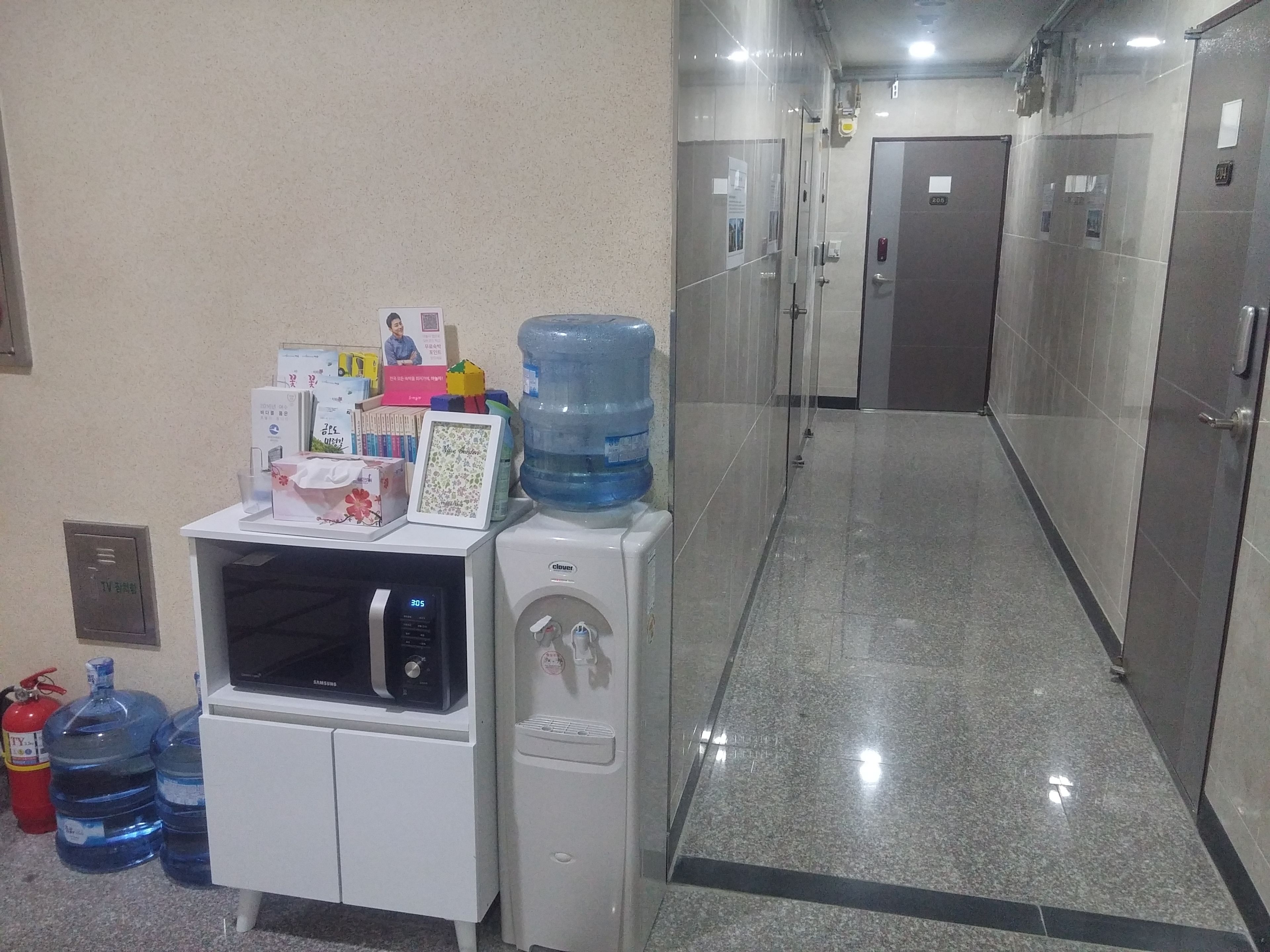 Corredor com micro-ondas, dispensador de água, extintor de incêndio e garrafas de água.