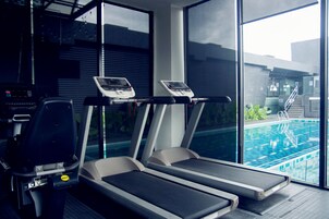 Uma academia com esteiras e piscina visíveis pelas janelas.