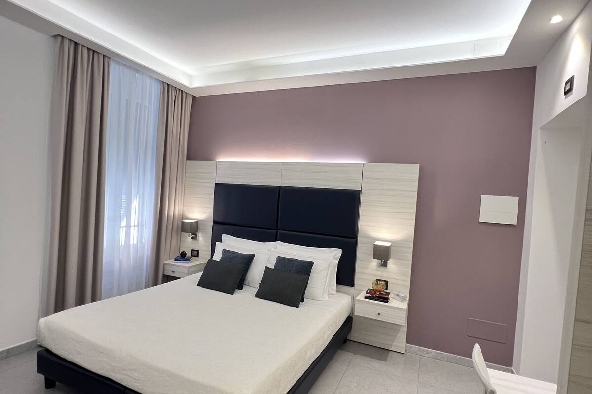 Quarto de hotel moderno com uma cama grande, mesas de cabeceira, uma escrivaninha e uma cadeira.