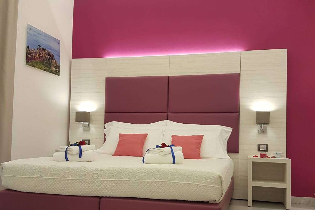 Quarto moderno com cama grande, paredes cor-de-rosa e luminária no teto.