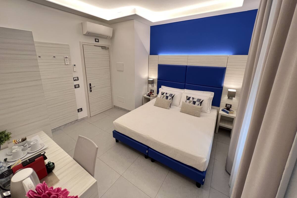 Um quarto moderno com uma cama grande, mesas de cabeceira, ar condicionado e uma escrivaninha com cadeira.