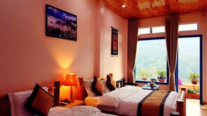Quarto de hotel com cama, mesa de cabeceira, abajur e vista para as montanhas pela janela.