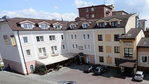 Um hotel com vários andares, uma área de estar coberta ao ar livre e diversos carros estacionados em frente.