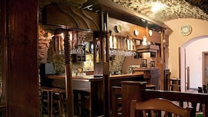 Uma área de bar rústica com mobiliário de madeira, paredes de pedra e diversos copos expostos em prateleiras.