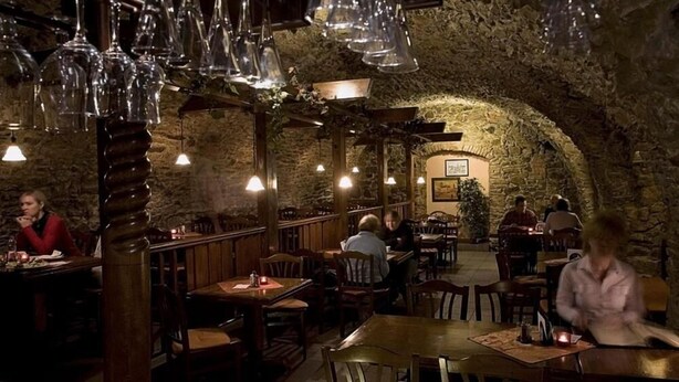 Um restaurante rústico com paredes de pedra, mesas de madeira e copos de vinho pendurados.