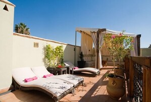 Terraço no telhado com duas espreguiçadeiras, um espaço coberto para sentar e plantas em vasos.