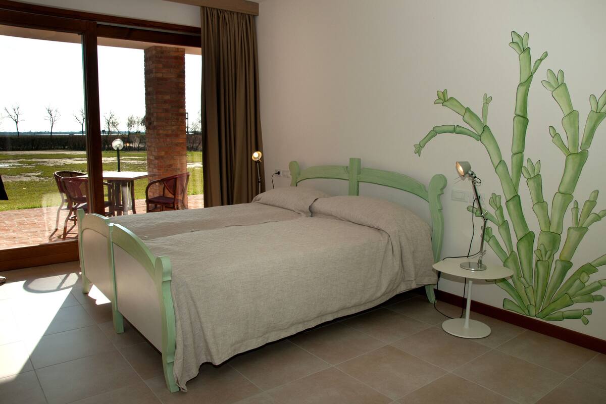 Quarto com cama, mesa, cadeiras e vista para o exterior.