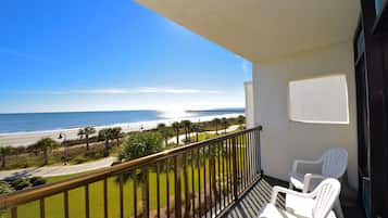Varanda com vista para a praia, cadeiras de plástico branco e um quadro branco na parede.
