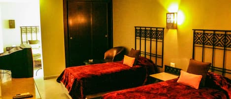 Quarto de hotel com duas camas, uma escrivaninha, uma cadeira e uma televisão.