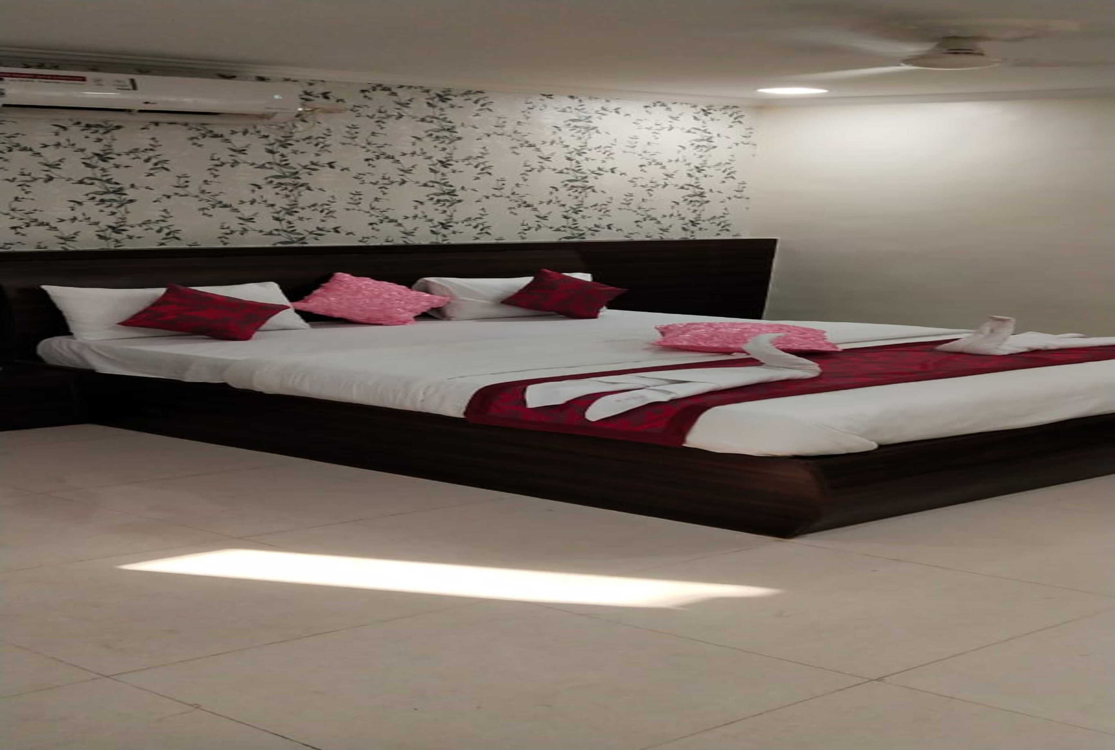 Cama bem arrumada com lençóis brancos e várias almofadas, cabeceira escura e parede com padrão floral.