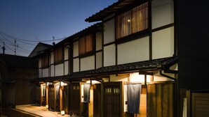 Um edifício tradicional japonês com vários quartos, cada um com uma porta deslizante e um pequeno candeeiro do lado de fora.