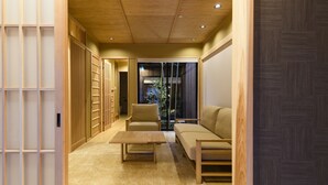 Quarto em estilo japonês tradicional, com portas deslizantes, sofá, mesa de centro e vista para o verde lá fora.