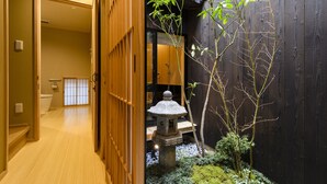 Interior japonês tradicional com soalho de madeira, um candeeiro de pedra e um pequeno jardim com musgo e plantas.