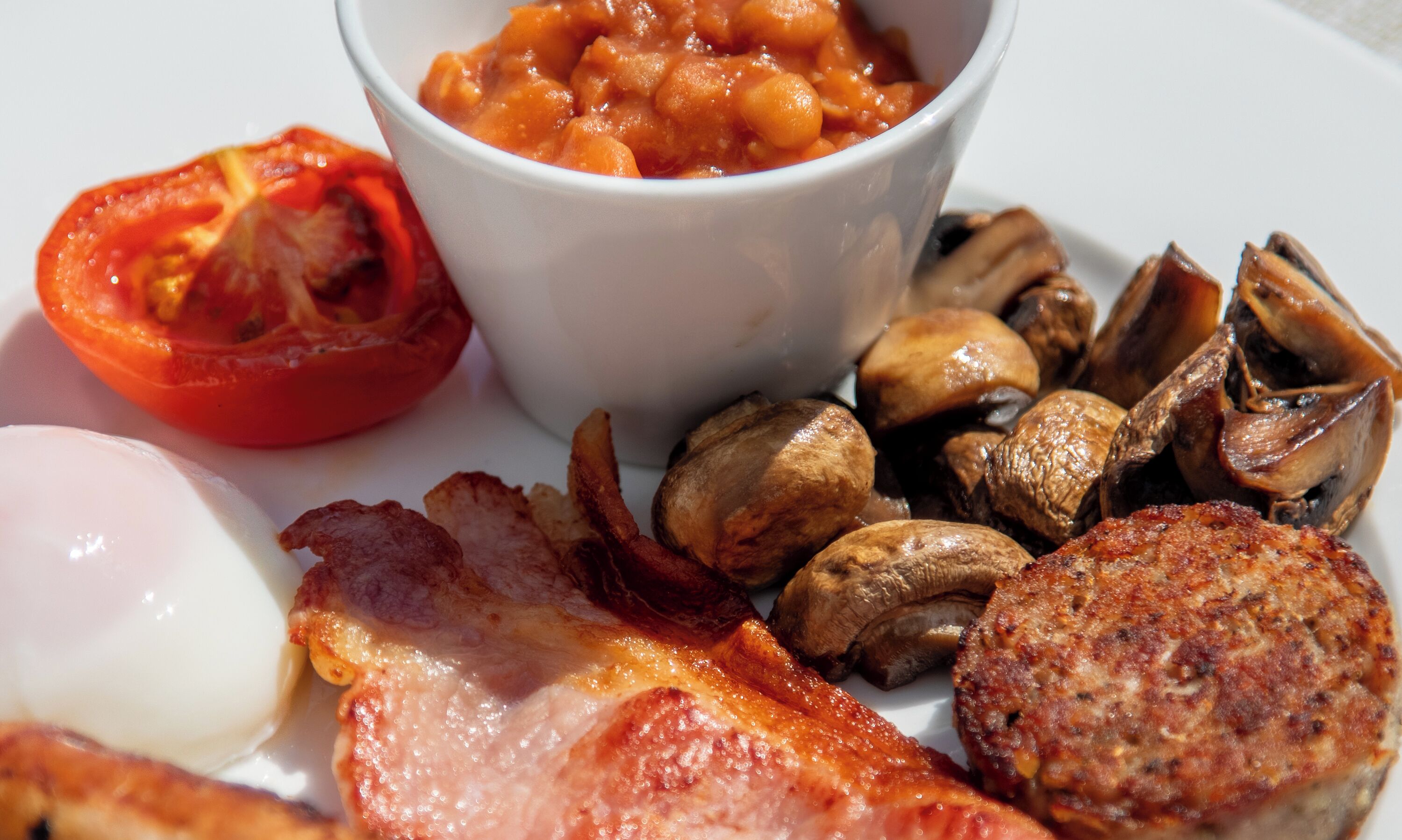 Prato de pequeno-almoço com ovos, bacon, cogumelos, feijão cozido e tomate.