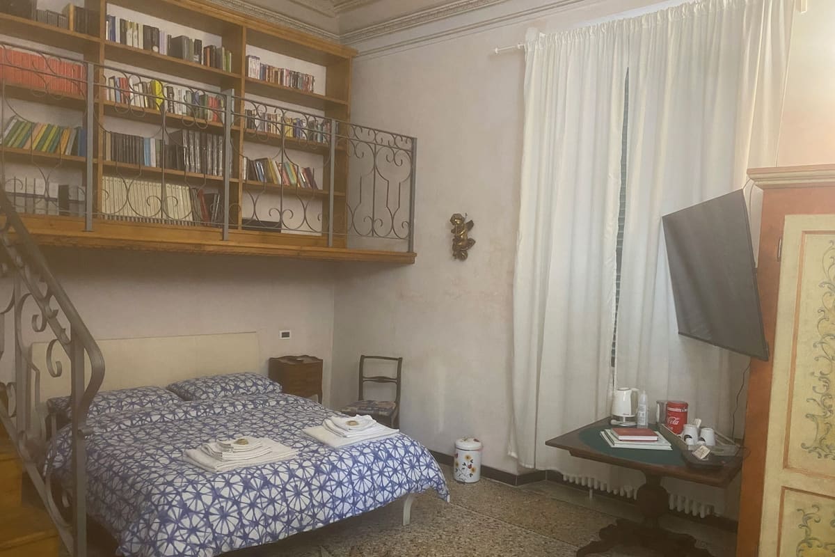 Quarto com cama, estante, mesa pequena com televisão e radiador.