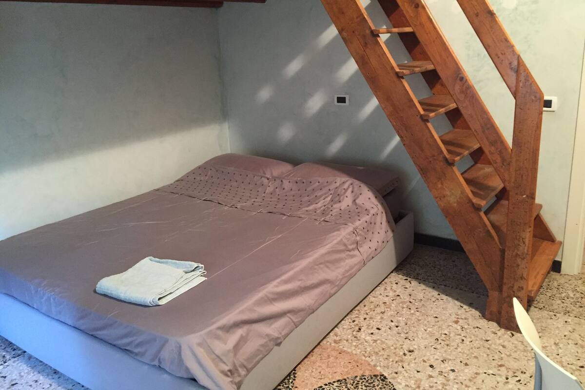 Uma cama de solteiro com uma escada de madeira em um quarto com teto inclinado.