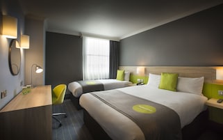 Quarto de hotel com duas camas, uma mesa, uma cadeira e janela com cortinas.