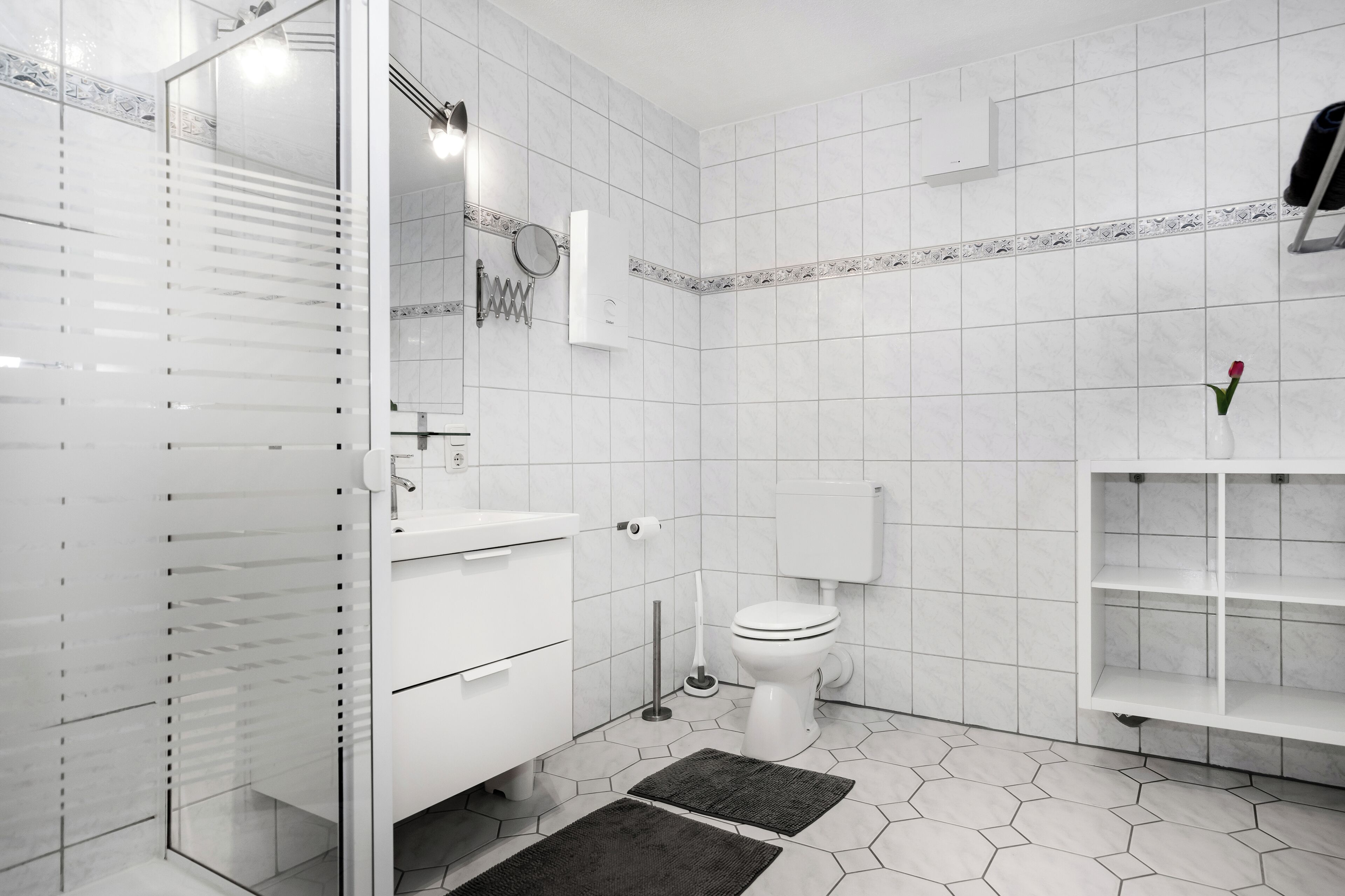 Um banheiro moderno com box de vidro, acessórios brancos e piso de azulejos hexagonais.