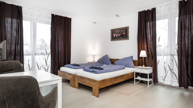 Quarto de hotel moderno com cama de madeira, duas mesas de cabeceira, uma escrivaninha e uma cadeira.