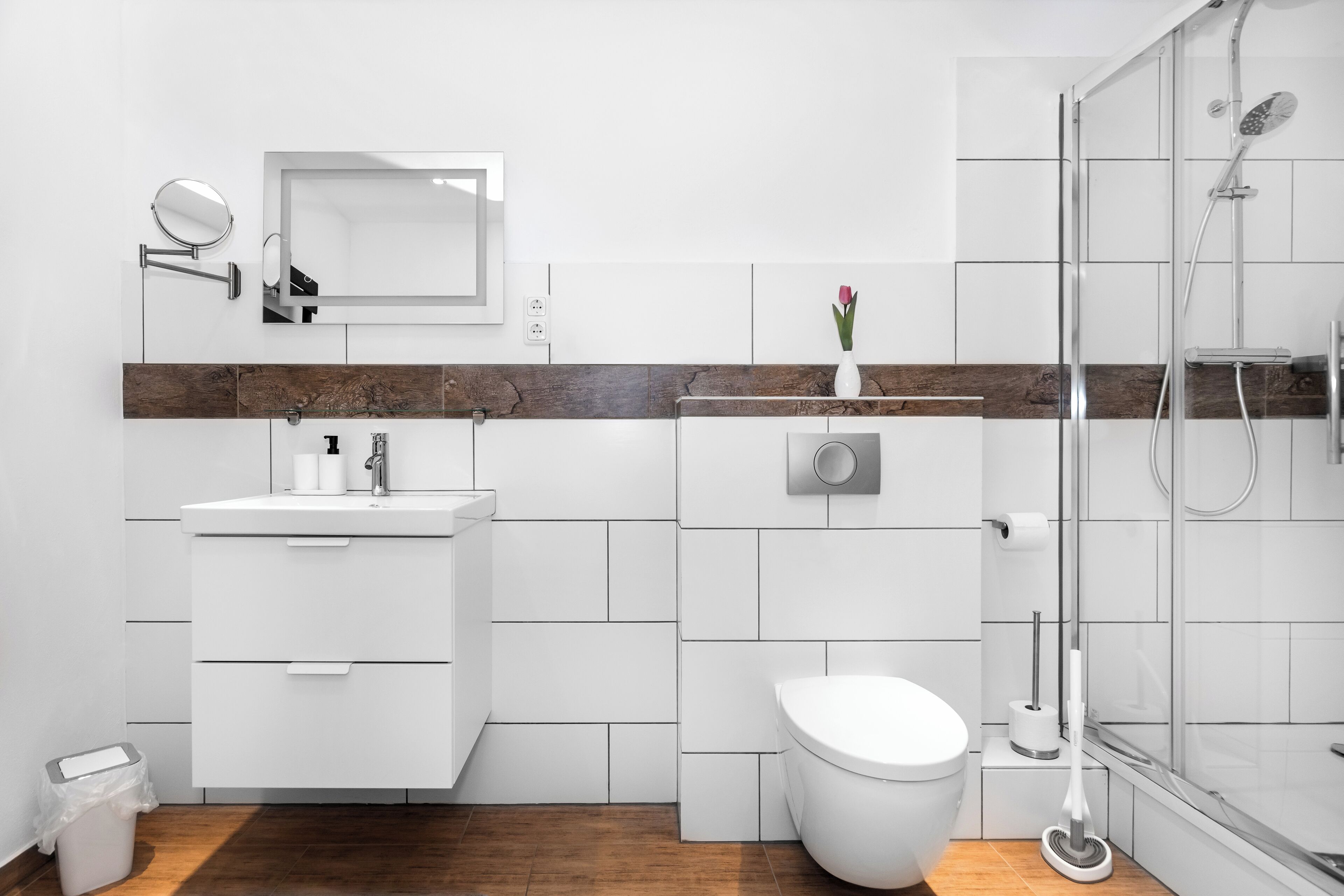 Casa de banho moderna com lavatório branco, espelho, sanita e chuveiro.