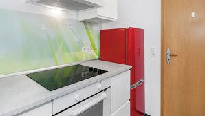 Uma cozinha compacta com um fogão por indução moderno, um forno embutido e uma geladeira vermelha.