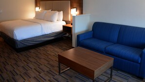 Quarto de hotel com uma cama, um sofá azul, uma mesa de centro de madeira e uma mesinha de cabeceira com abajur.