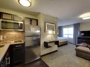 Quarto de hotel moderno com cozinha compacta, uma cama, televisão e sofá.